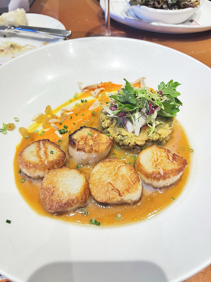 Perfectly seared scallops surrounding a throne of risotto &ndash; each caramelized medallion is like ocean butter with a golden crust that sings of culinary precision.