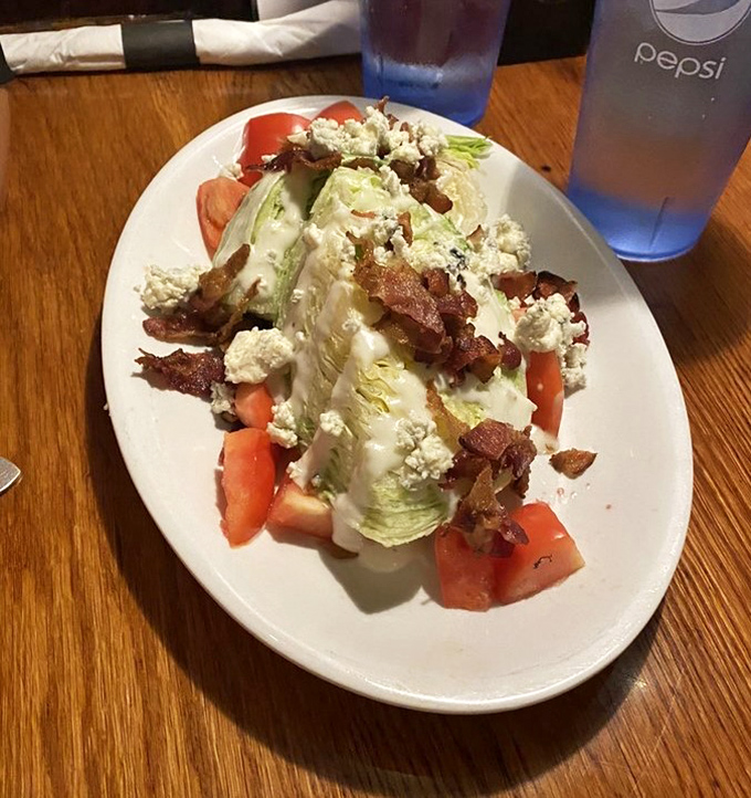 The wedge salad stands tall and proud, bacon bits scattered like confetti at a celebration of blue cheese and fresh vegetables.