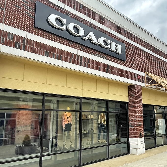 The Coach sign stands proud against brick and cream, a beacon for those seeking leather luxury without the Manhattan price tag.