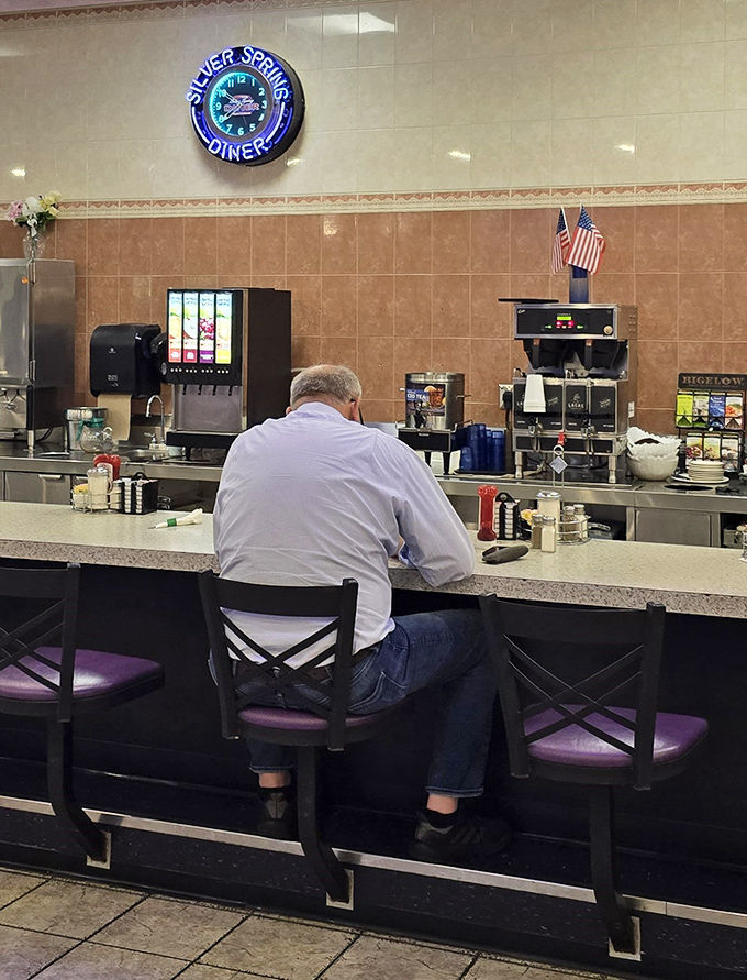 The counter where solo diners find community. That neon clock isn't just telling time&mdash;it's telling stories of late-night conversations and early morning revelations.