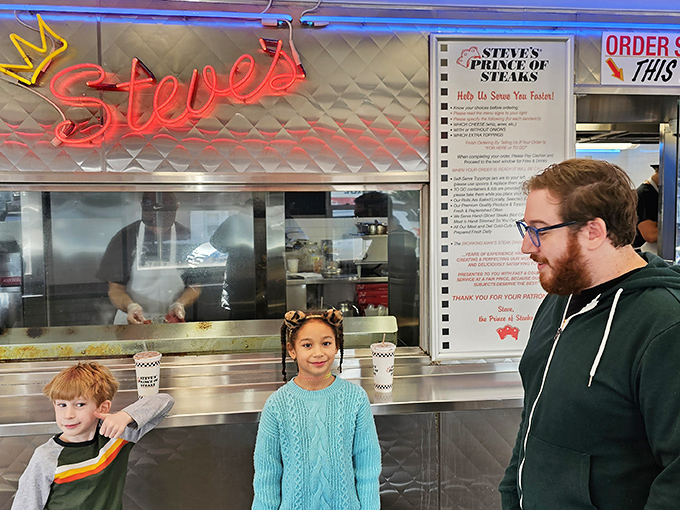 The pilgrimage in progress. Families passing down Philly food traditions while the neon "Steve's" sign bathes everything in a warm glow.