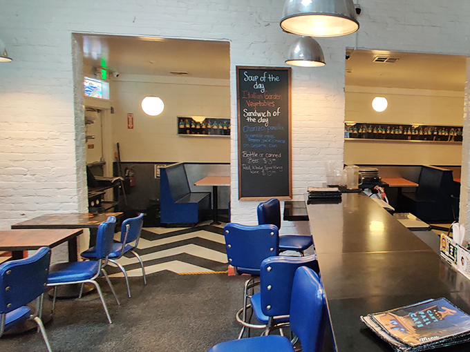 The chalkboard announces daily specials like breaking news, while blue chairs wait patiently for the next round of hungry philosophers and hungover musicians.