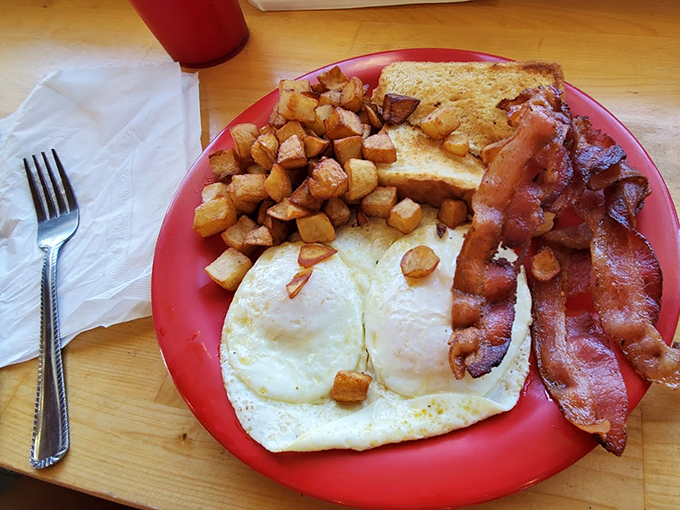 The breakfast trinity: eggs, bacon, and potatoes, arranged with the reverence they deserve. Simple perfection on a red plate&mdash;no filter needed, just hunger.