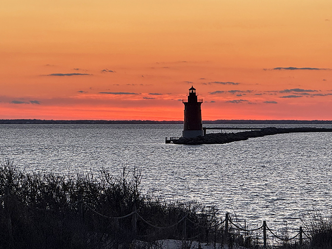 The lighthouse silhouette against a fiery sunset sky creates the kind of moment that makes amateur photographers look like professionals.