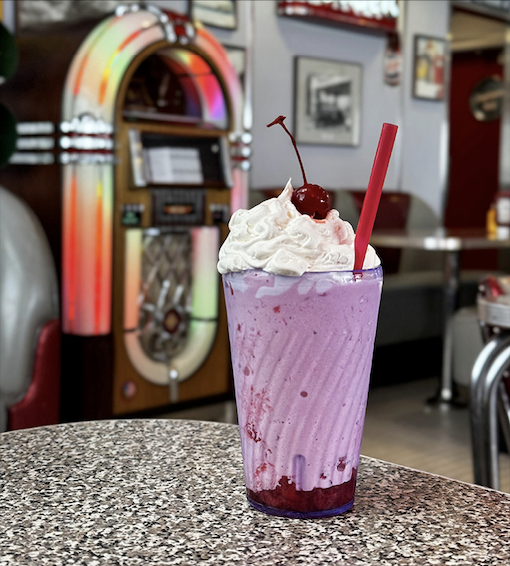 A strawberry milkshake that belongs in the Dessert Hall of Fame, complete with whipped cream mountain and cherry on top.