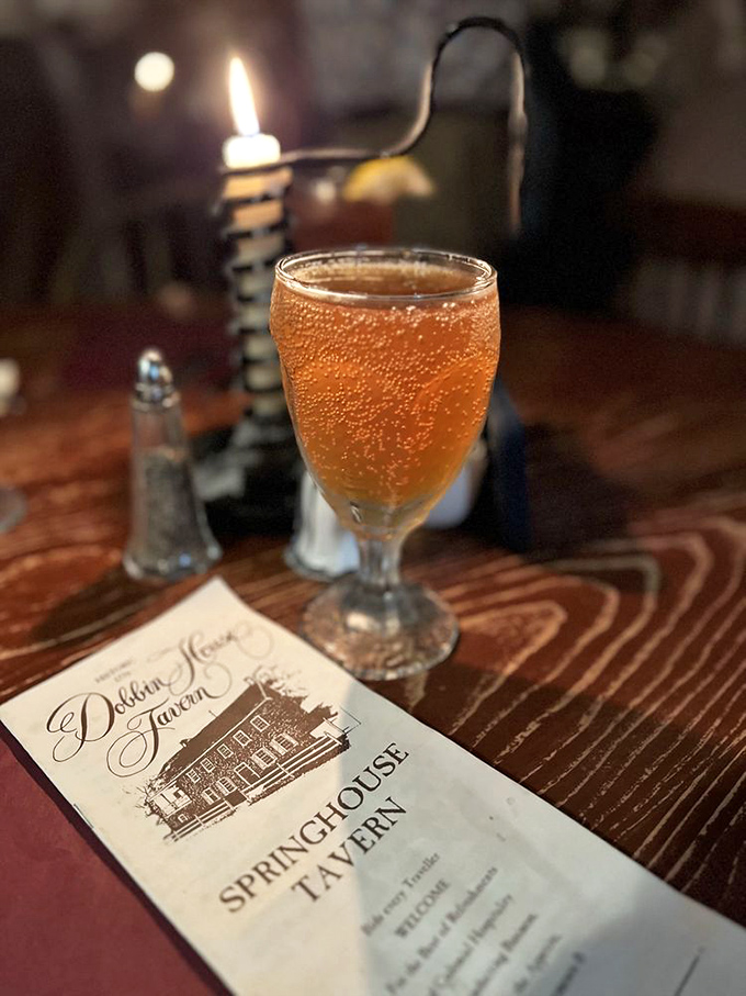 In the glow of candlelight, a colonial-era beverage awaits beside a menu promising historic flavors in this atmospheric tavern setting.