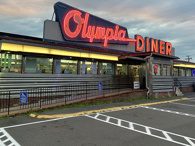 As dusk settles, the Olympia's neon sign transforms into a glowing red invitation &ndash; like a lighthouse guiding ships of hungry patrons to safe, delicious harbor.