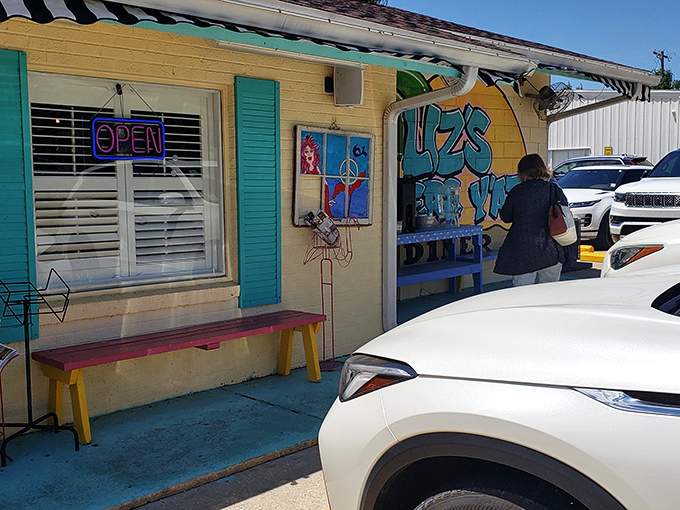 The cheerful exterior of Liz's Where Y'at Diner welcomes hungry visitors with its vibrant mural and colorful bench—breakfast paradise found!