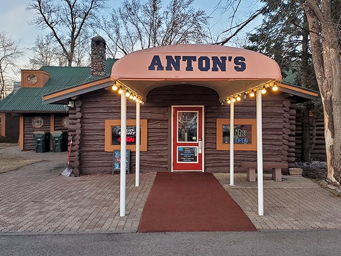 The rustic log cabin exterior of Anton's beckons like a warm hug on a cold Minnesota evening. That red door practically whispers, "Come on in, the steaks are waiting."