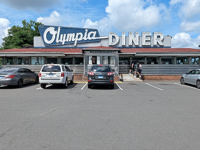 The iconic Olympia Diner sign stands proudly against Connecticut's blue sky, a beacon of comfort food that's been calling hungry travelers home for generations.