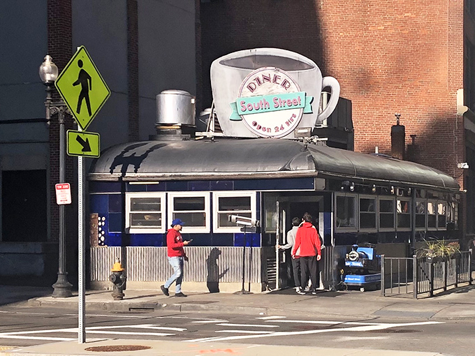 Sunlight illuminates the classic diner structure as patrons approach Boston's beloved round-the-clock eatery under its famous cup sign.