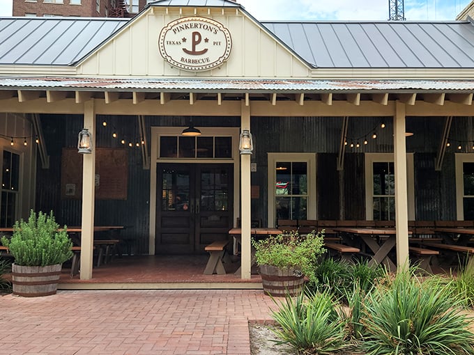 Pinkerton's classic Texas exterior beckons with rustic charm and string lights, promising smoky treasures within. The "P" logo stands as a beacon for barbecue pilgrims.
