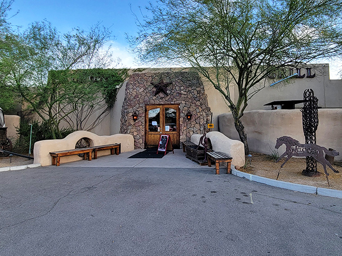 The adobe entrance to San Tan Flat stands like a portal to the Old West, complete with rustic benches and a metal horse silhouette standing guard.