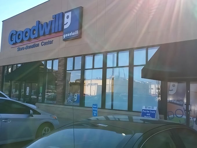 The blue Goodwill sign beckons like a lighthouse for bargain hunters. Behind these unassuming doors lies a wonderland of possibilities and second chances.