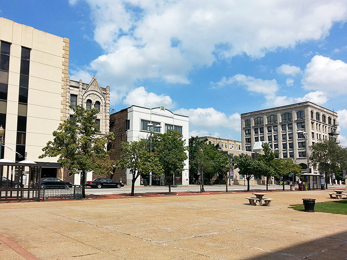 Downtown Joliet's public square offers a peaceful urban oasis surrounded by historic architecture and modern buildings under bright blue skies.