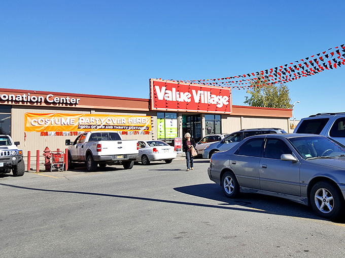 The iconic red Value Village sign welcomes treasure hunters under classic Alaskan blue skies, colorful pennants fluttering like flags at a perpetual celebration of secondhand finds.