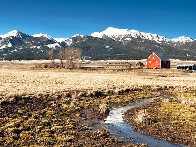 A red barn stands proudly with towering mountains as its backdrop, evoking a sense of Oregon's gold rush era and whispering tales of boom times and frontier dreams.