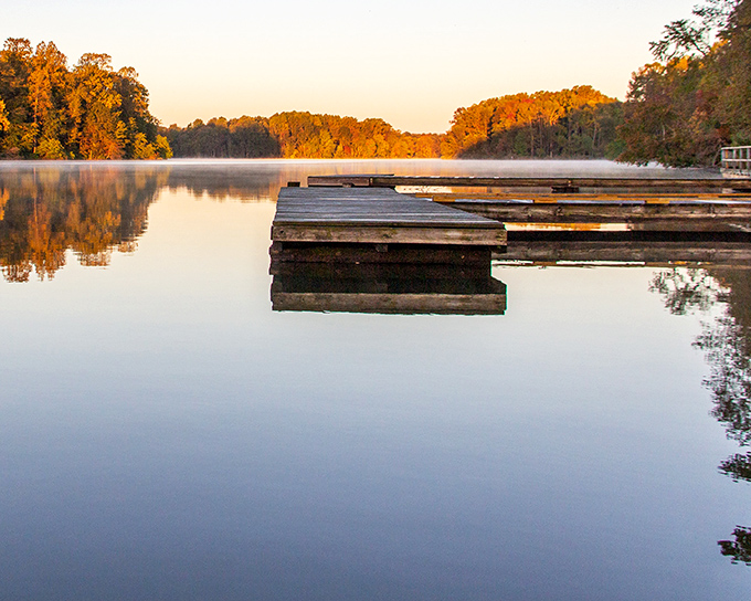 Golden autumn sunrise bathes Lums Pond in perfect stillness, with weathered docks awaiting the day's first visitors.