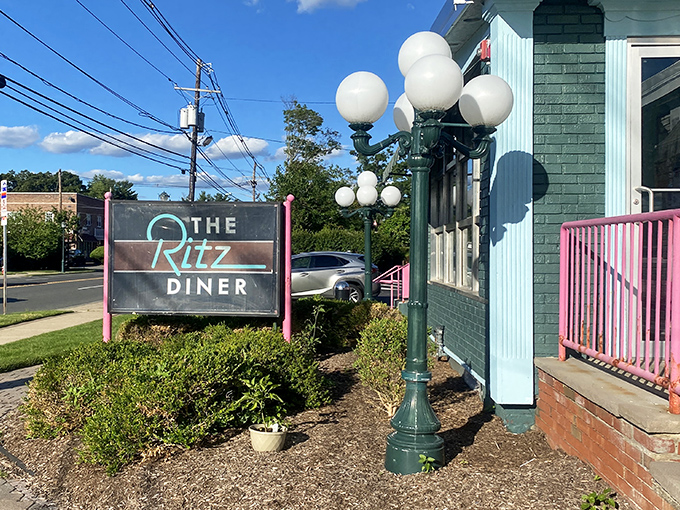 The teal and pink exterior of the Ritz Diner stands like a time capsule from a more affordable era, welcoming hungry patrons with retro charm.