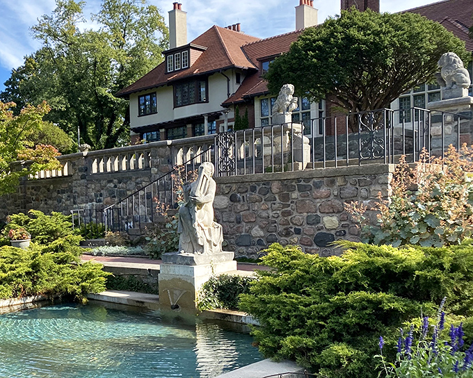 The Tudor-style mansion rises from its garden setting like a storybook come to life, complete with reflecting pool and classical statuary that whispers of old-world elegance.