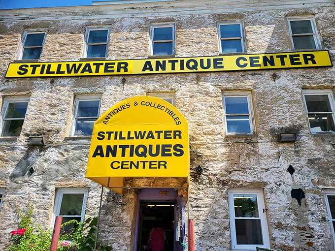 The historic stone mill building houses Stillwater Antique Center, where that bright yellow sign practically screams "treasures inside!" like a beacon for curious souls.
