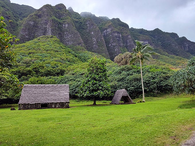 Traditional Hawaiian structures nestled beneath dramatic mountain ridges – where ancient wisdom meets jaw-dropping natural beauty in perfect harmony.