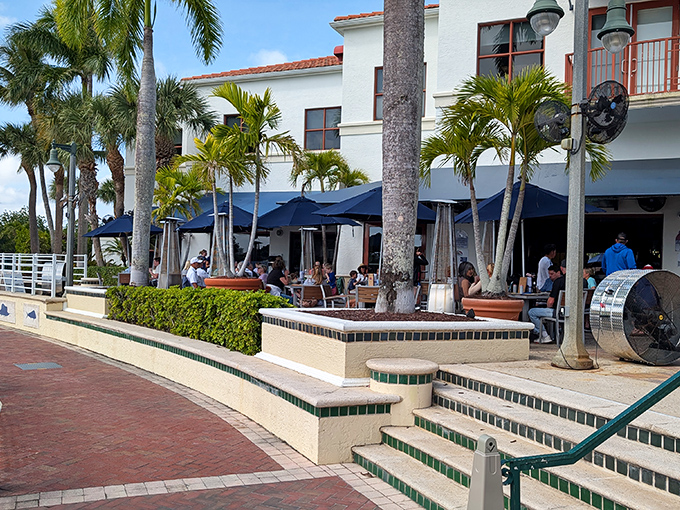 A lively Florida waterfront restaurant with blue umbrellas, palm trees, and relaxed outdoor dining by the marina.