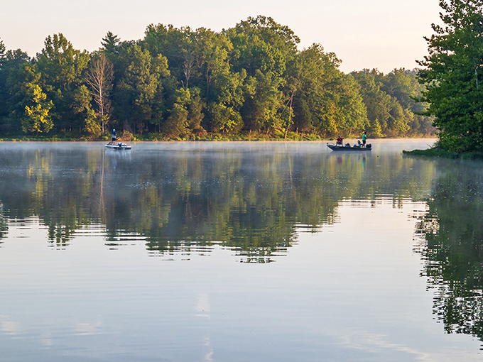 Morning mist rises off Kincaid Lake as fishing boats glide through waters so still they mirror the sky perfectly.