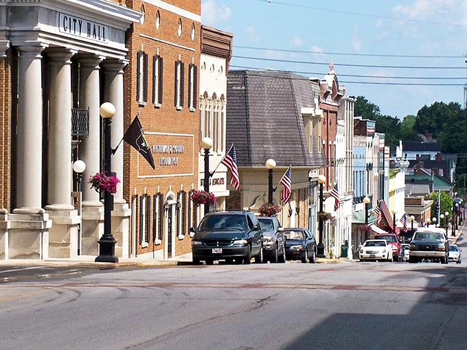 Historic City Hall anchors a charming small-town Main Street adorned with American flags and summer blooms.