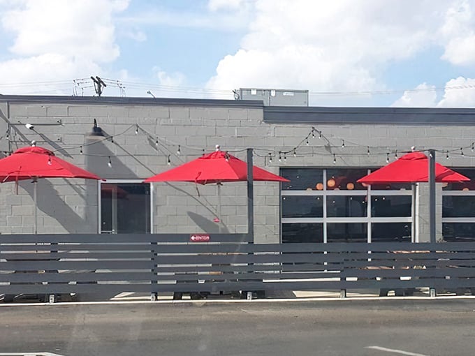 The unassuming exterior of Old Scratch Pizza, where those vibrant red umbrellas hint at the colorful culinary experience waiting inside.
