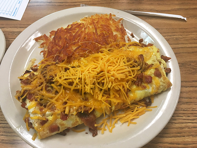 This isn't just an omelet—it's a cheese-covered canvas of breakfast artistry with a supporting cast of perfectly crisped hash browns.