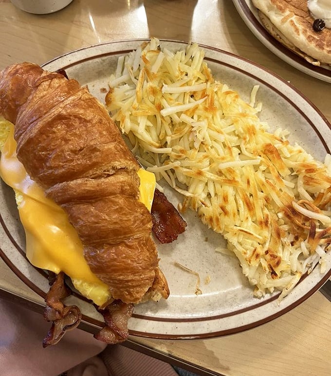 The breakfast croissant sandwich &ndash; where buttery pastry meets morning classics. Those hash browns are playing the long game of perfect crispiness.