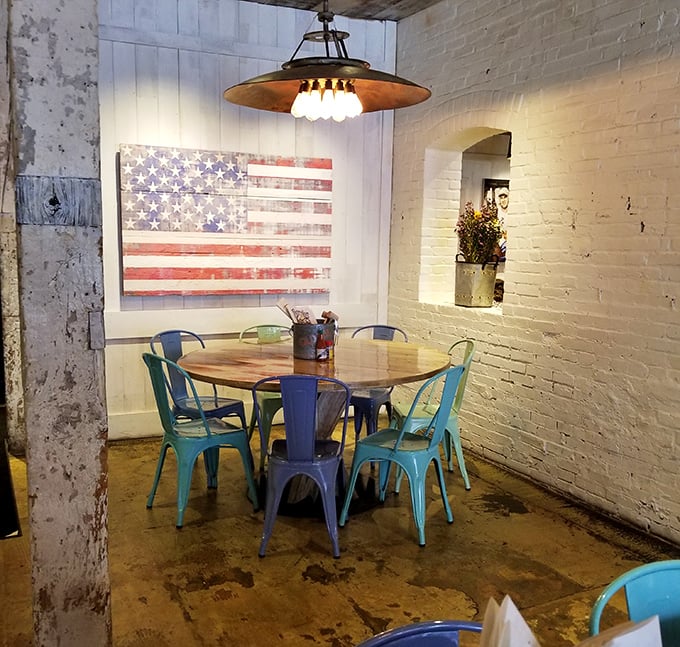 American flag art watches over colorful metal chairs and weathered wood. Like Captain America designed a dining space after visiting Brooklyn.