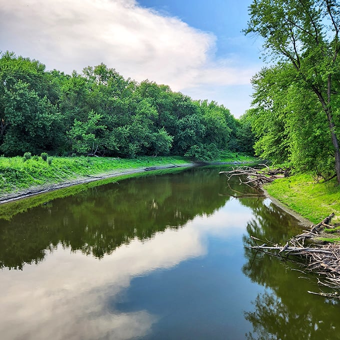 Mirror-like waters double the beauty of this serene river scene, reflecting clouds and greenery in nature's most perfect symmetry.