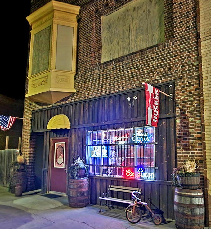 Night transforms this unassuming storefront into a neon-lit oasis of Nebraska nightlife, where barrel planters and vintage charm create unexpected small-town ambiance.