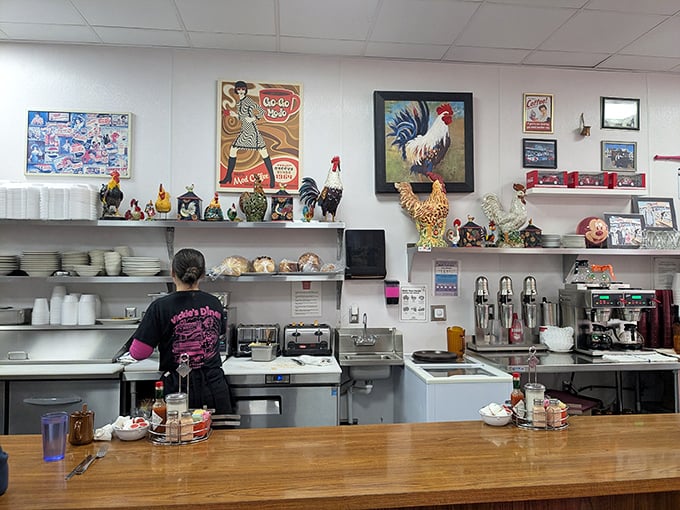 Behind the counter, where diner magic happens &ndash; note the rooster collection watching over proceedings like feathered guardians of breakfast tradition.