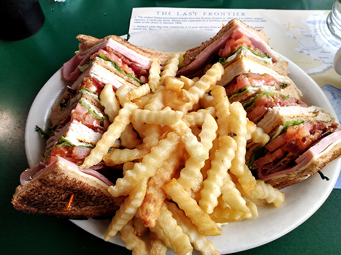 This club sandwich stands tall and proud, layers stacked with military precision, surrounded by a golden regiment of crispy fries standing guard.