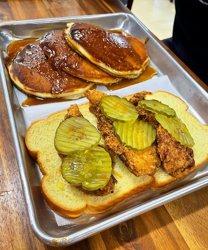 Breakfast meets lunch in this metal tray of joy&mdash;crispy chicken on white bread with pickles alongside pancakes drowning happily in syrup.
