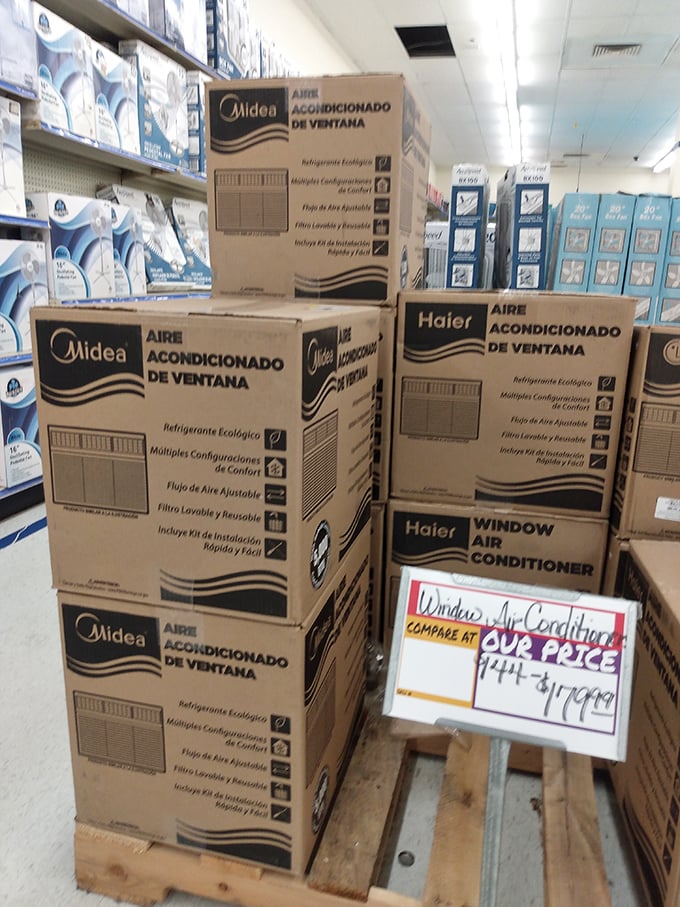 Window air conditioners stacked like cool promises of summer relief, with handwritten price comparisons that speak to old-school retail honesty.