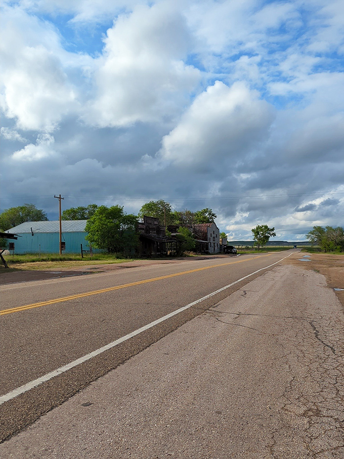 The open road cuts through Scenic like a timeline, with weathered buildings on one side and endless prairie on the other.