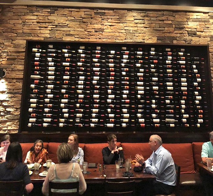 Good conversation flows as freely as the wine at these tables. The stone wall and wine display create an atmosphere where lingering is encouraged.