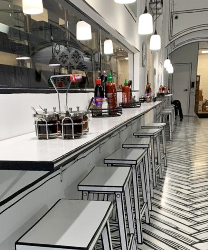 The counter seating offers front-row tickets to the culinary show, with colorful condiments playing supporting roles against the stark backdrop.