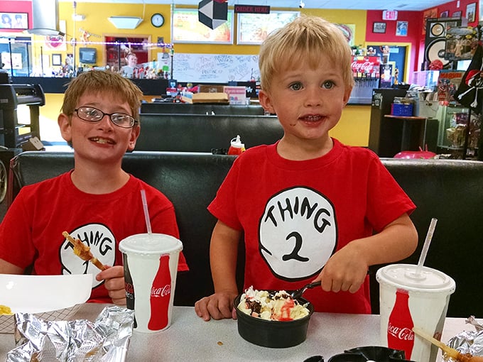 The image shows two young customers enjoying their meal at DogMahal DogHaus. Their expressions capture the simple joy that comes from good food in a fun environment.