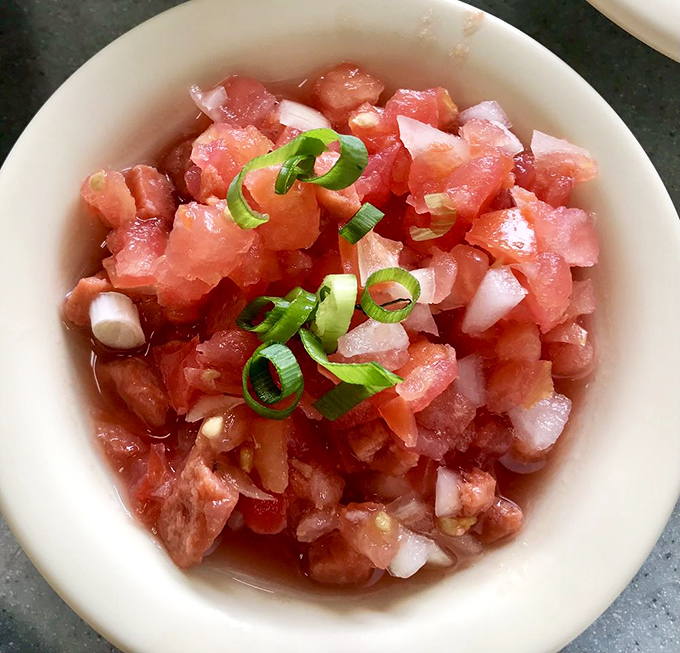 Lomi salmon dances with freshness &ndash; diced salmon, tomatoes, and onions create a bright, refreshing counterpoint to the meal's richer elements.