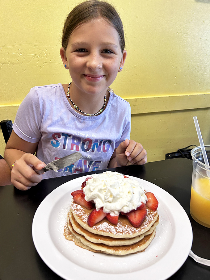 A young diner enjoying pancakes topped with strawberries and whipped cream. The look of breakfast joy is universal and ageless.