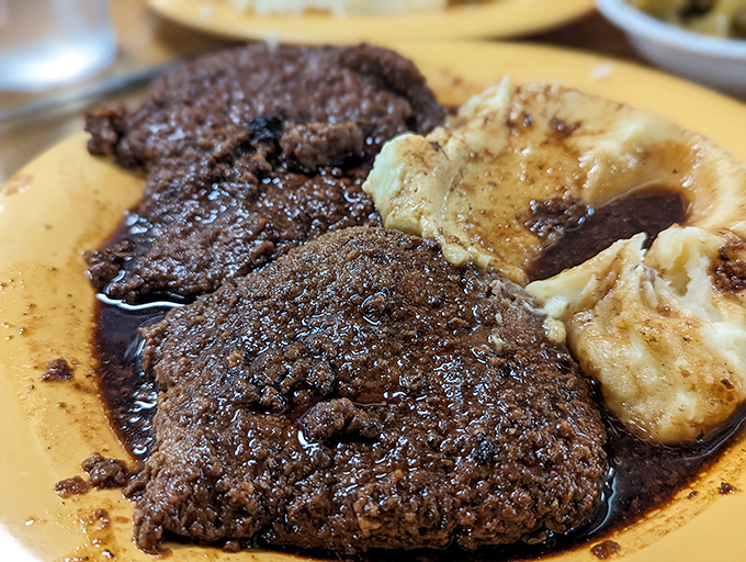 Salisbury steak swimming in rich brown gravy alongside mashed potatoes &ndash; comfort food engineering at its most scientifically delicious.