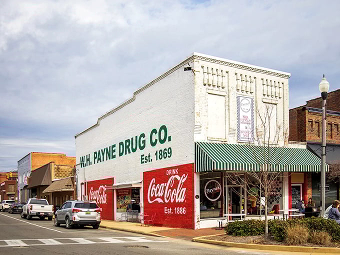 Scottsboro's W.H. Payne Drug Co. stands proudly since 1869, a white-brick testament to small-town permanence. Coca-Cola signs hint at simpler pleasures inside.