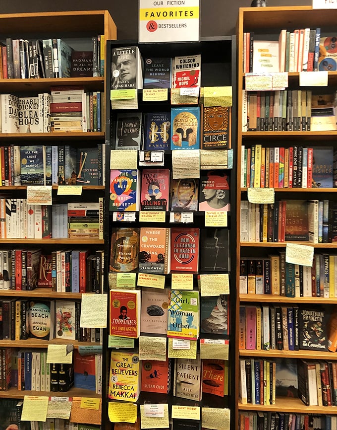 The "Fiction Favorites" wall&mdash;where handwritten yellow notes transform browsing into intimate conversations with passionate readers who've gone before you.