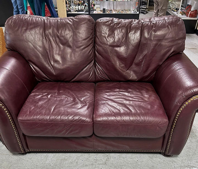 This burgundy leather loveseat has seen things, my friend. With its brass studs and well-worn cushions, it's practically begging to tell its stories.