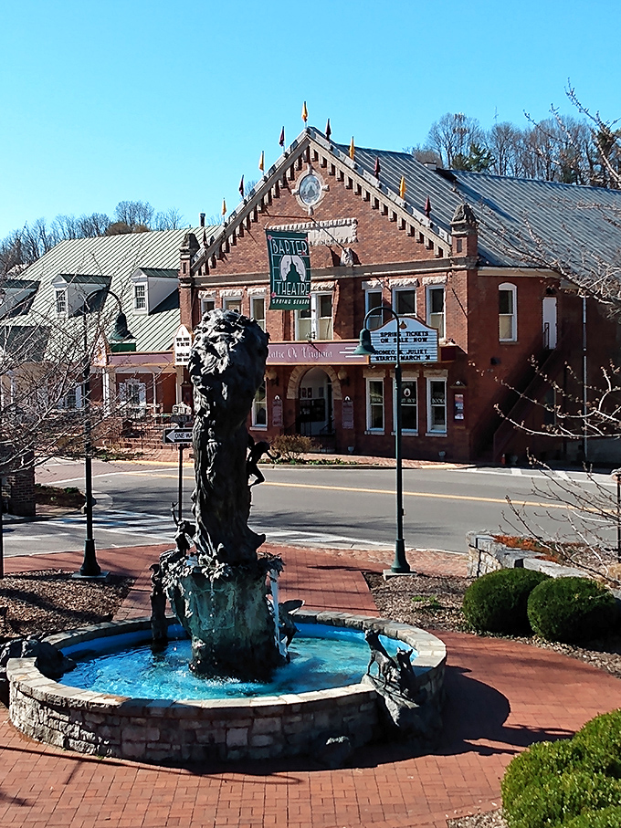The historic Barter Theatre stands proudly in downtown Abingdon, Virginia, with its distinctive brick facade and metal roof, while a beautiful fountain adds charm to the brick-paved courtyard in the foreground.